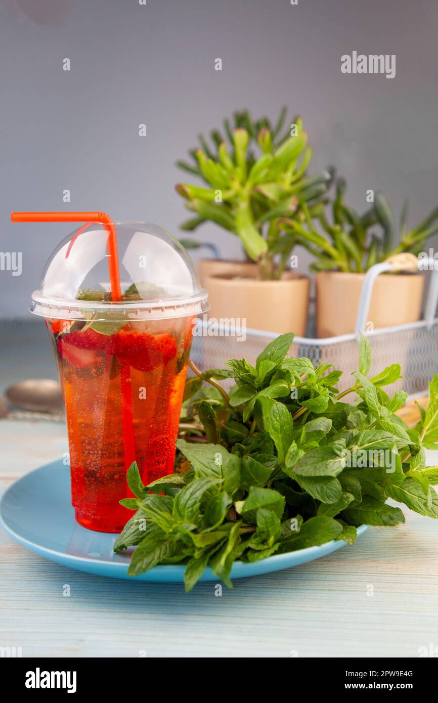 Summer mint strawberry refreshing cocktail mojito with ice in plastic glass with straw ...