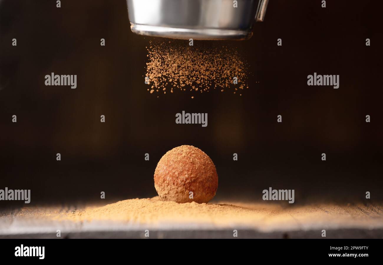 A ball of chocolate truffle is sprinkled with cocoa from a sieve on a ...