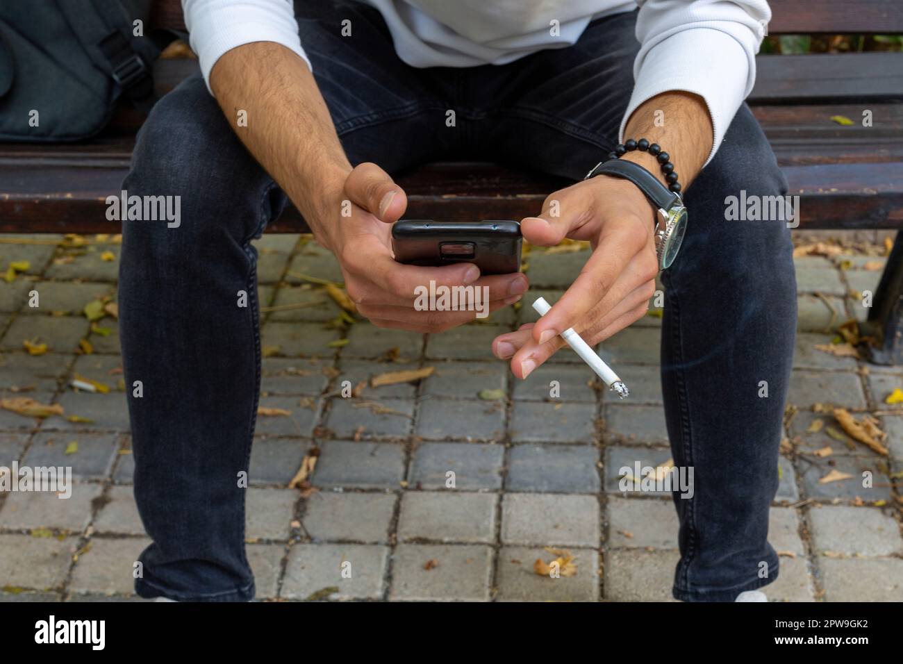 Young man smoking a cigarette, phone in hand Stock Photo - Alamy