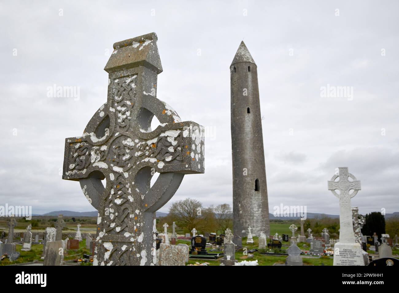 celtic cross in the graveyard of Kilmacduagh monastery with round tower ...