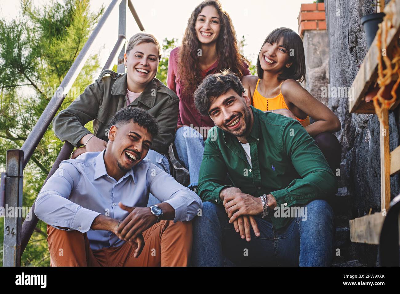 A group of five diverse friends posing on a staircase at sunset in a ...