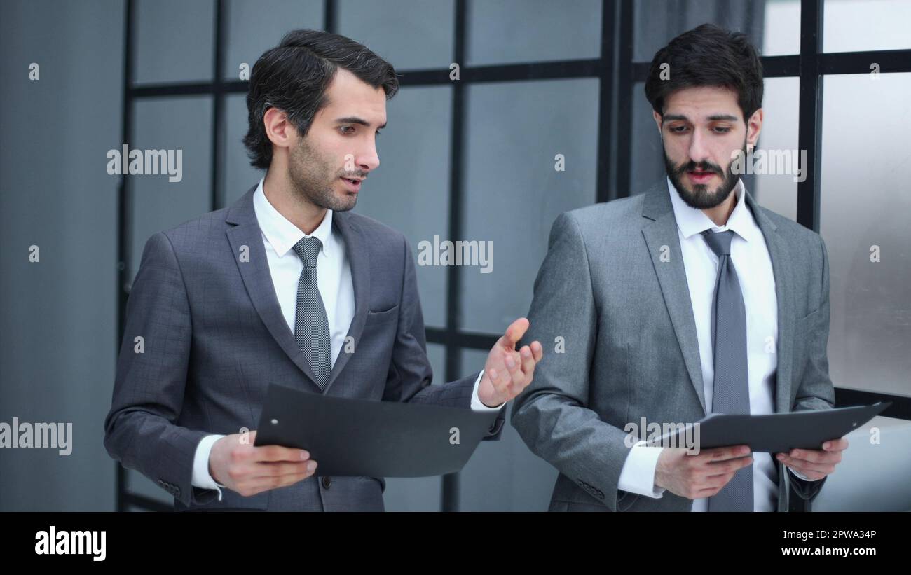 Rear view of two businessmen as they stare out a large window with a ...