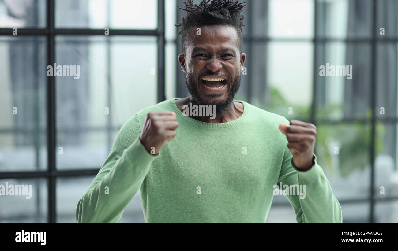 Winning ecstatic young African man clenching his fists with excited ...