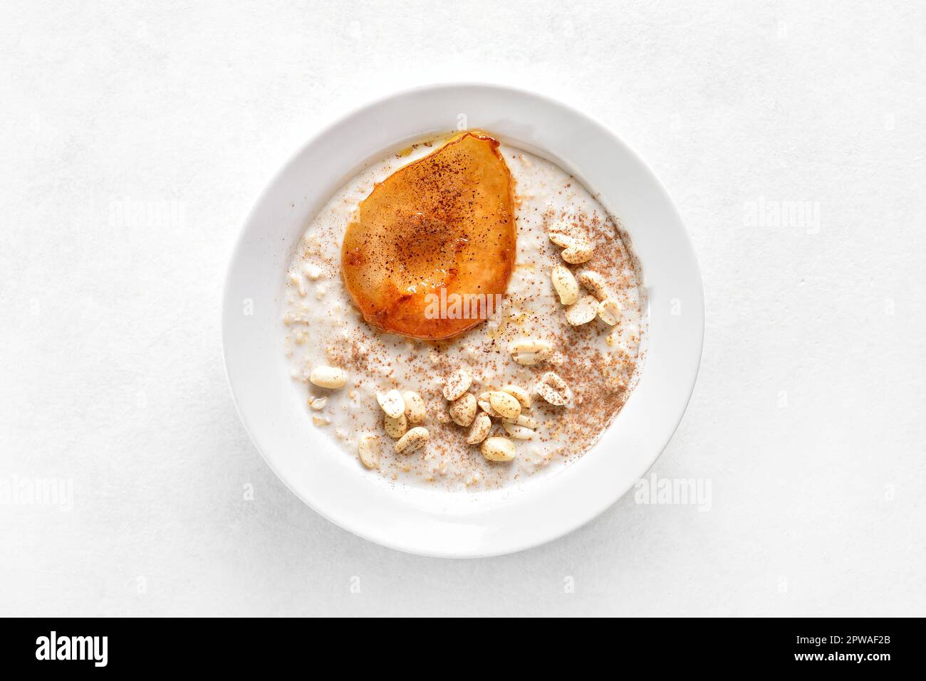 Oat porridge with caramelized pear and peanut in bowl over white ...
