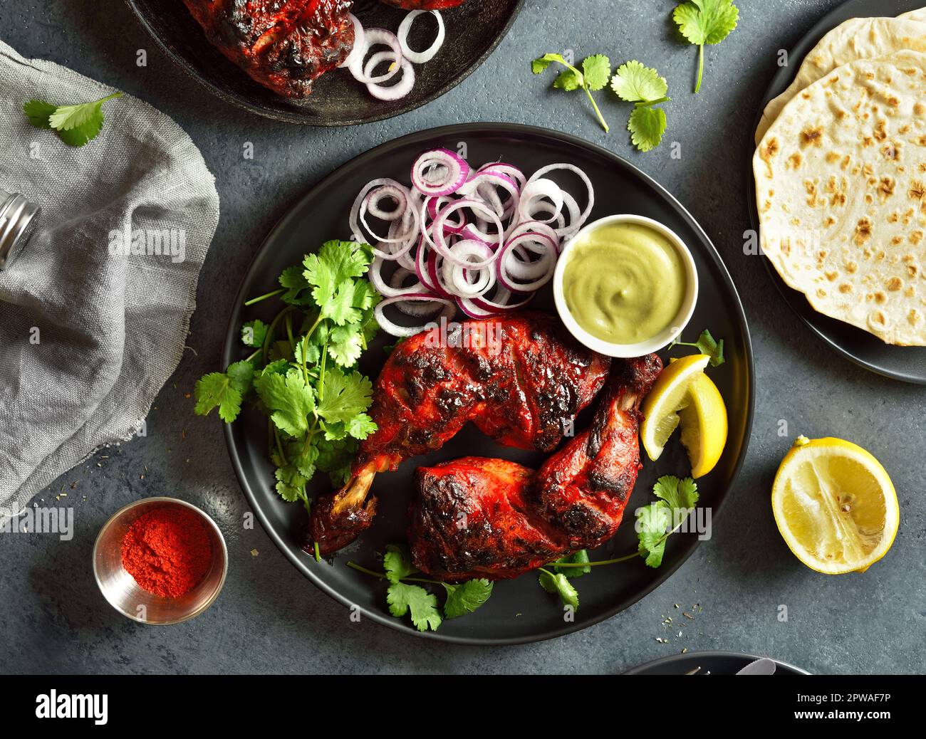 Tandoori chicken served with cilantro and onion on plate over dark ...