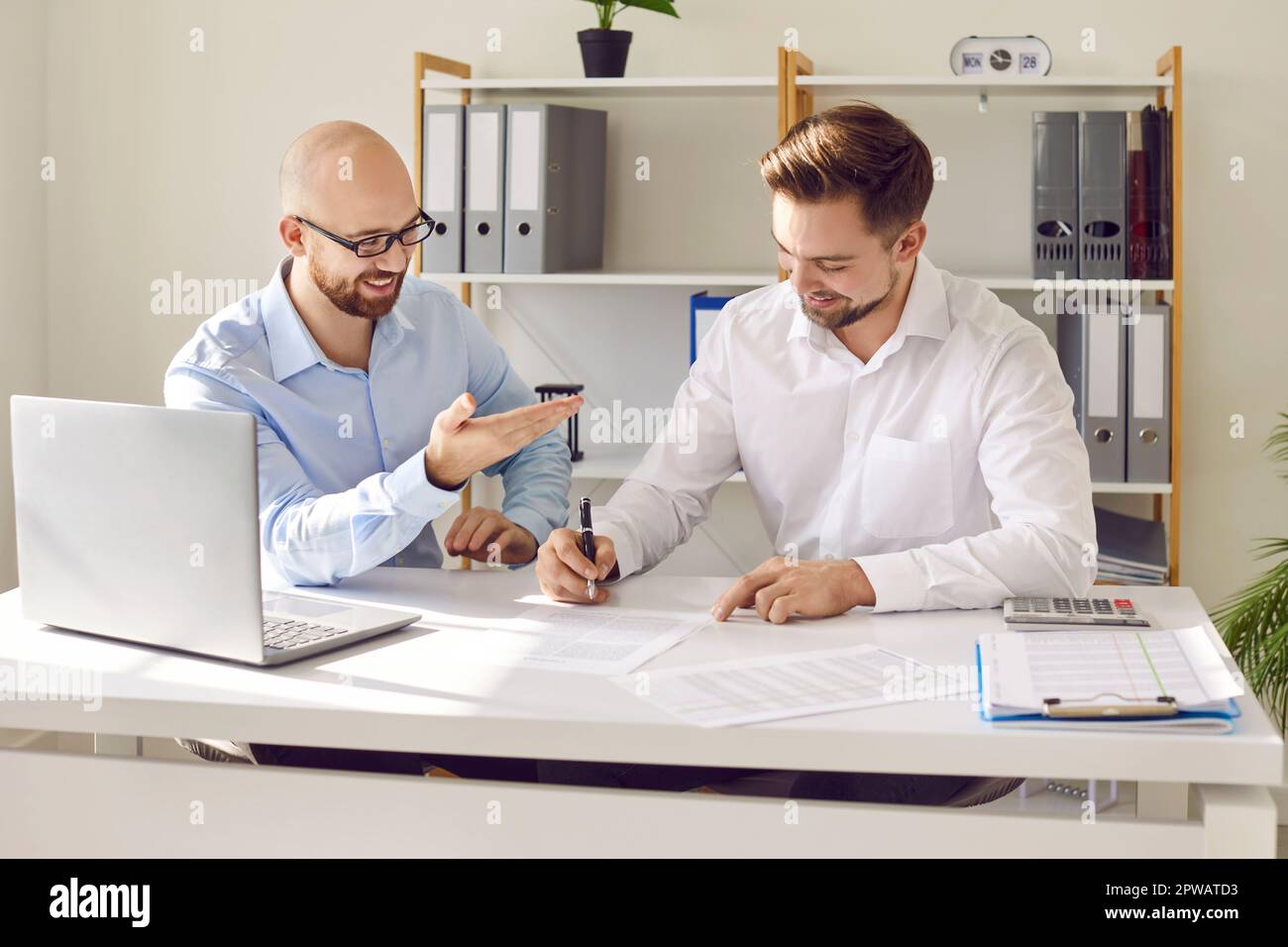 Two smiling business men at work in office talking, reaching agreement ...
