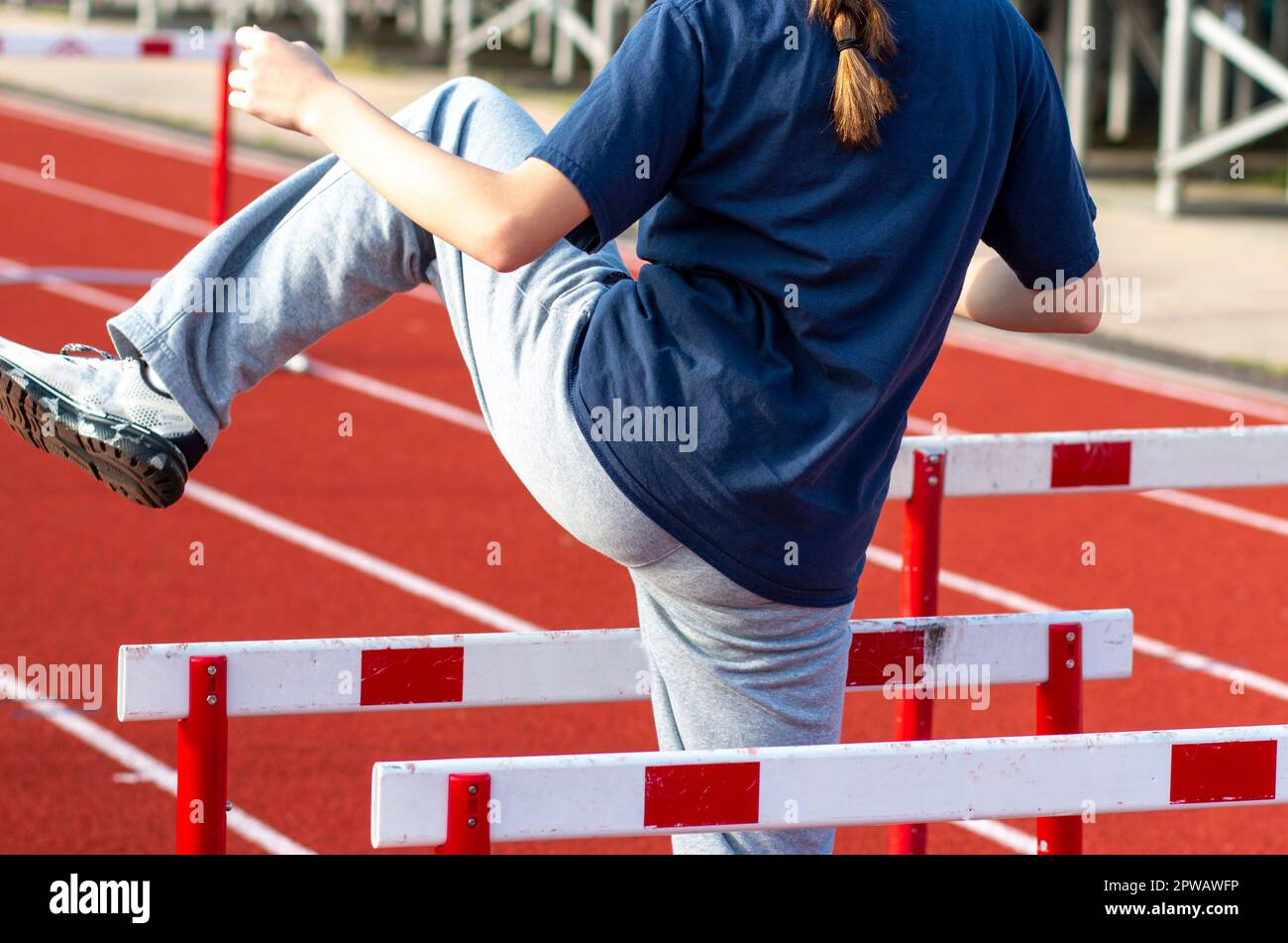 Rear view of a high school girl walking over track hurdles warming up ...