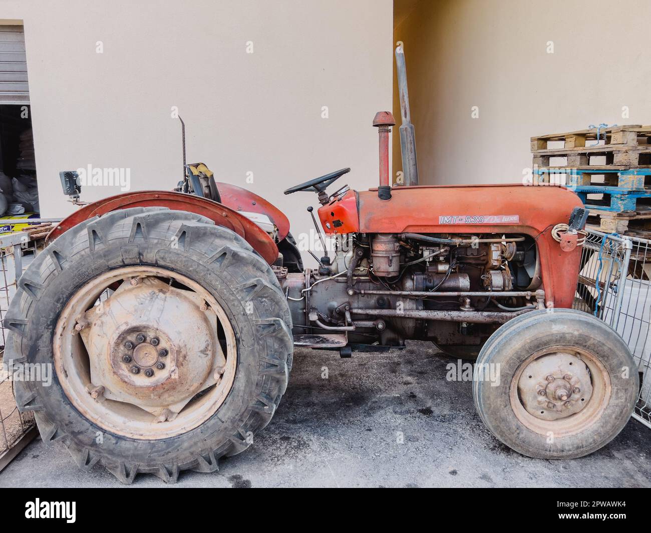 Small old red metal minitractor stands against the wall of a building ...