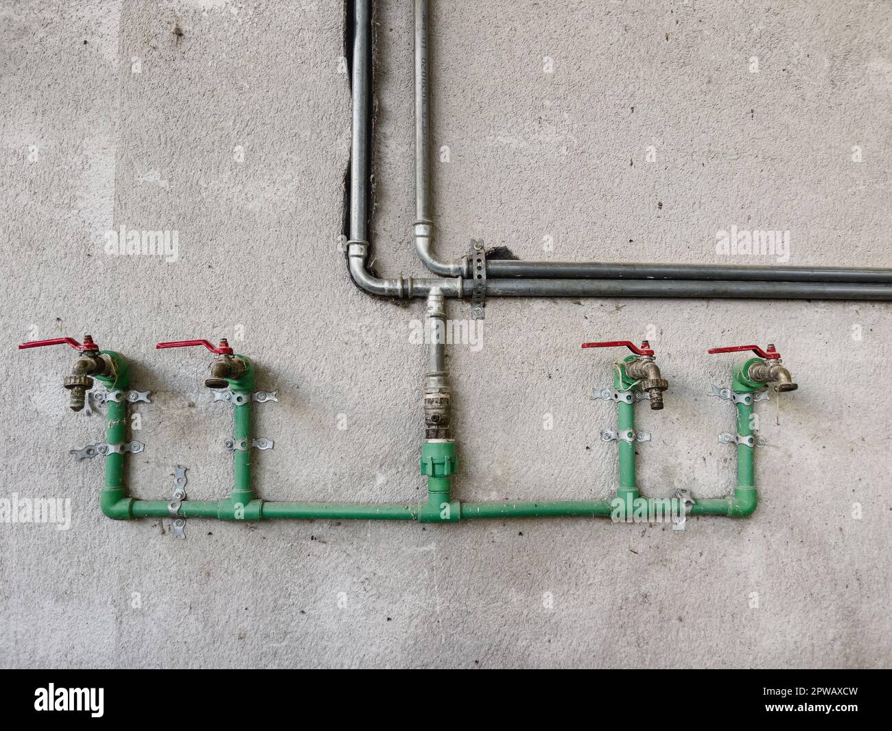 Distribution of water taps on a concrete wall next to pipes Stock Photo ...