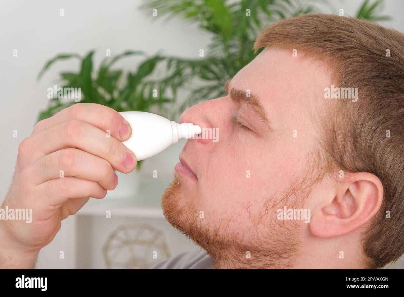 An adult male uses a nasal spray to relieve a runny nose. The concept ...