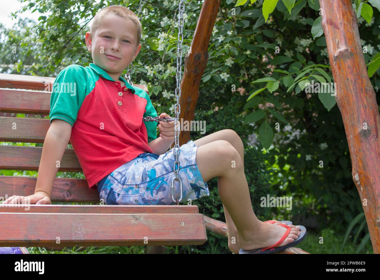 boy in shorts sitting on a wooden swing Stock Photo - Alamy