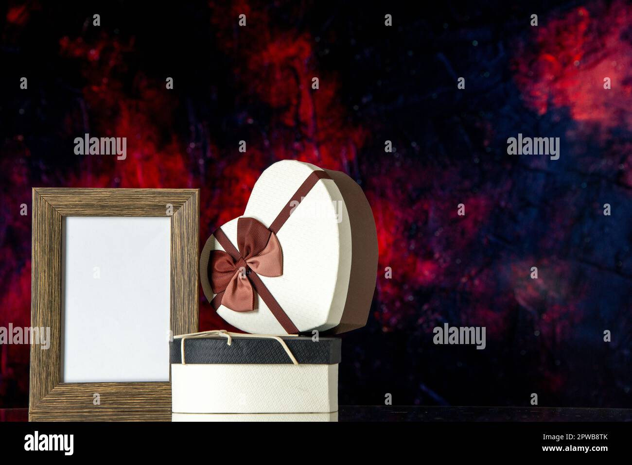 front view valentines day presents with empty picture frame on dark red ...