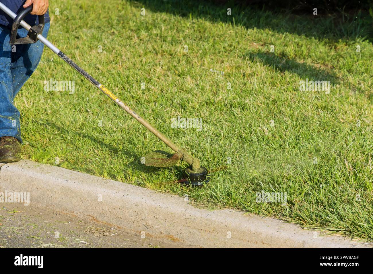 Municipal worker with lawn mower mows fresh green grass near road using ...