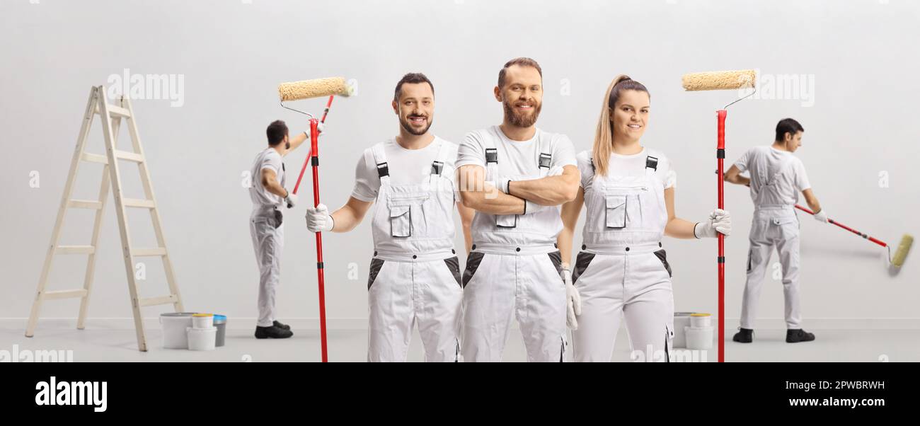 House decorators standing and looking at camera and other painting a ...