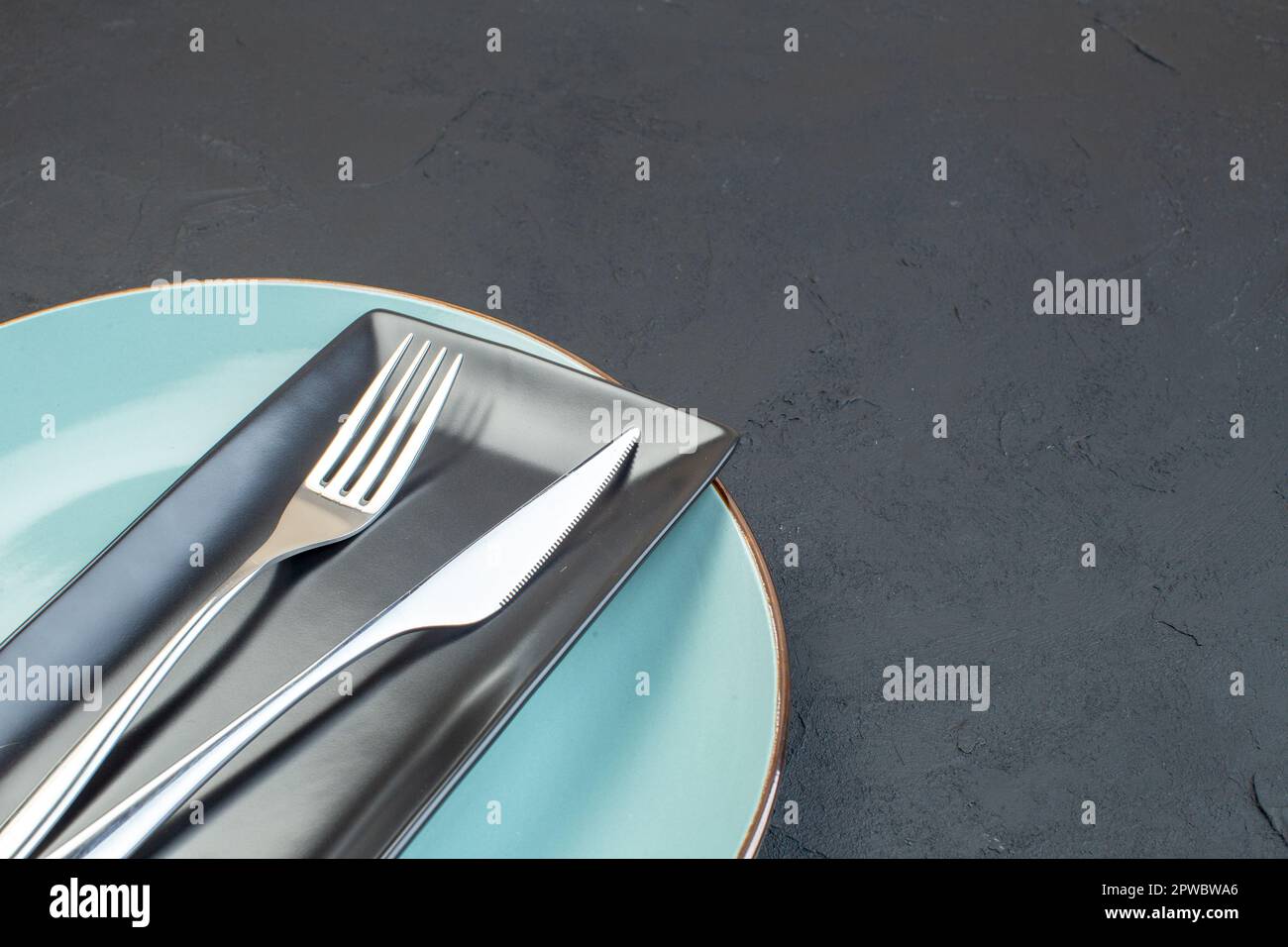 front view long black plate with blue plate fork and knife on dark ...