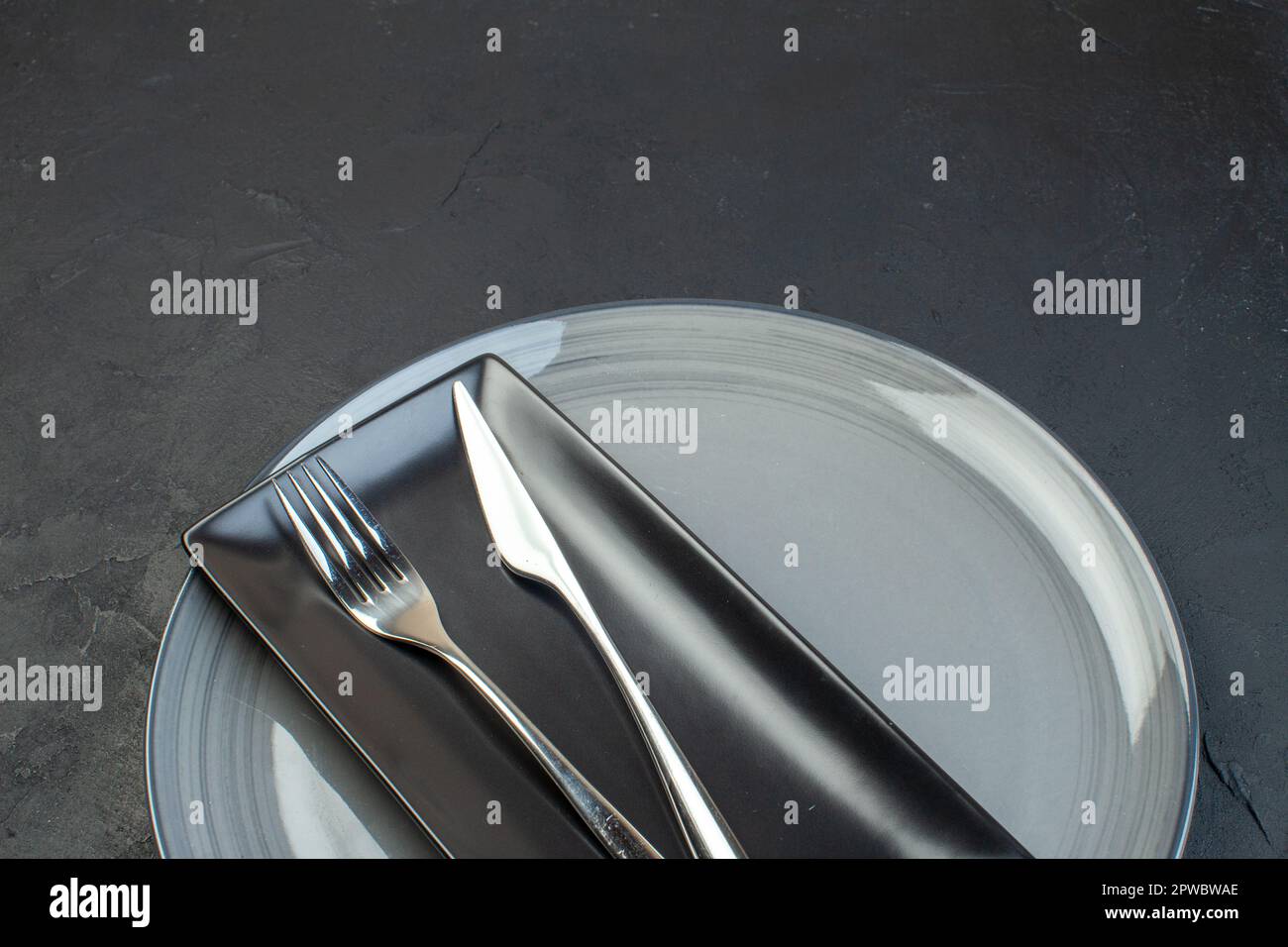 front view long black plate with fork and knife in gray plate on dark ...
