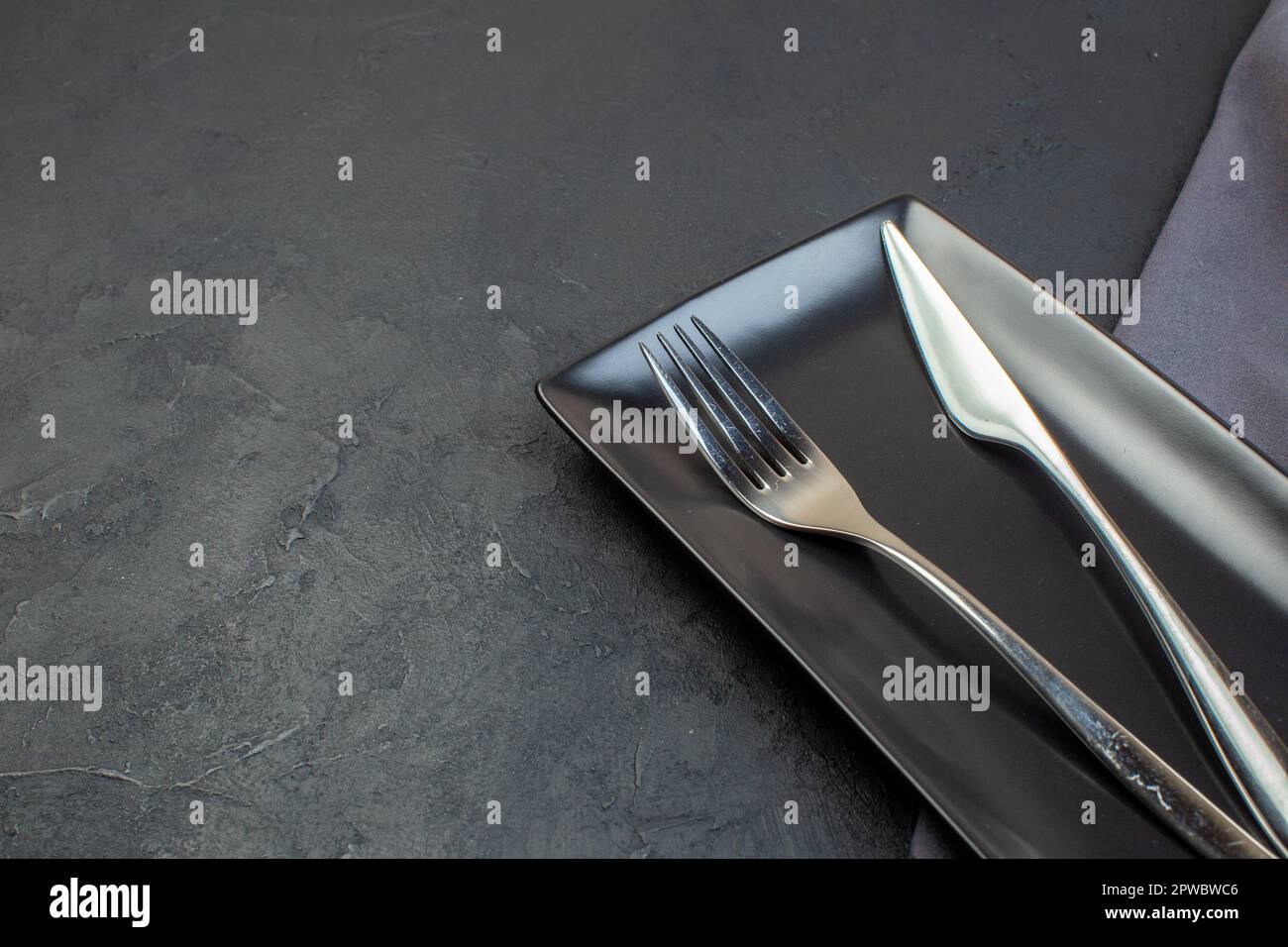 front view long black plate with fork and knife inside on dark ...