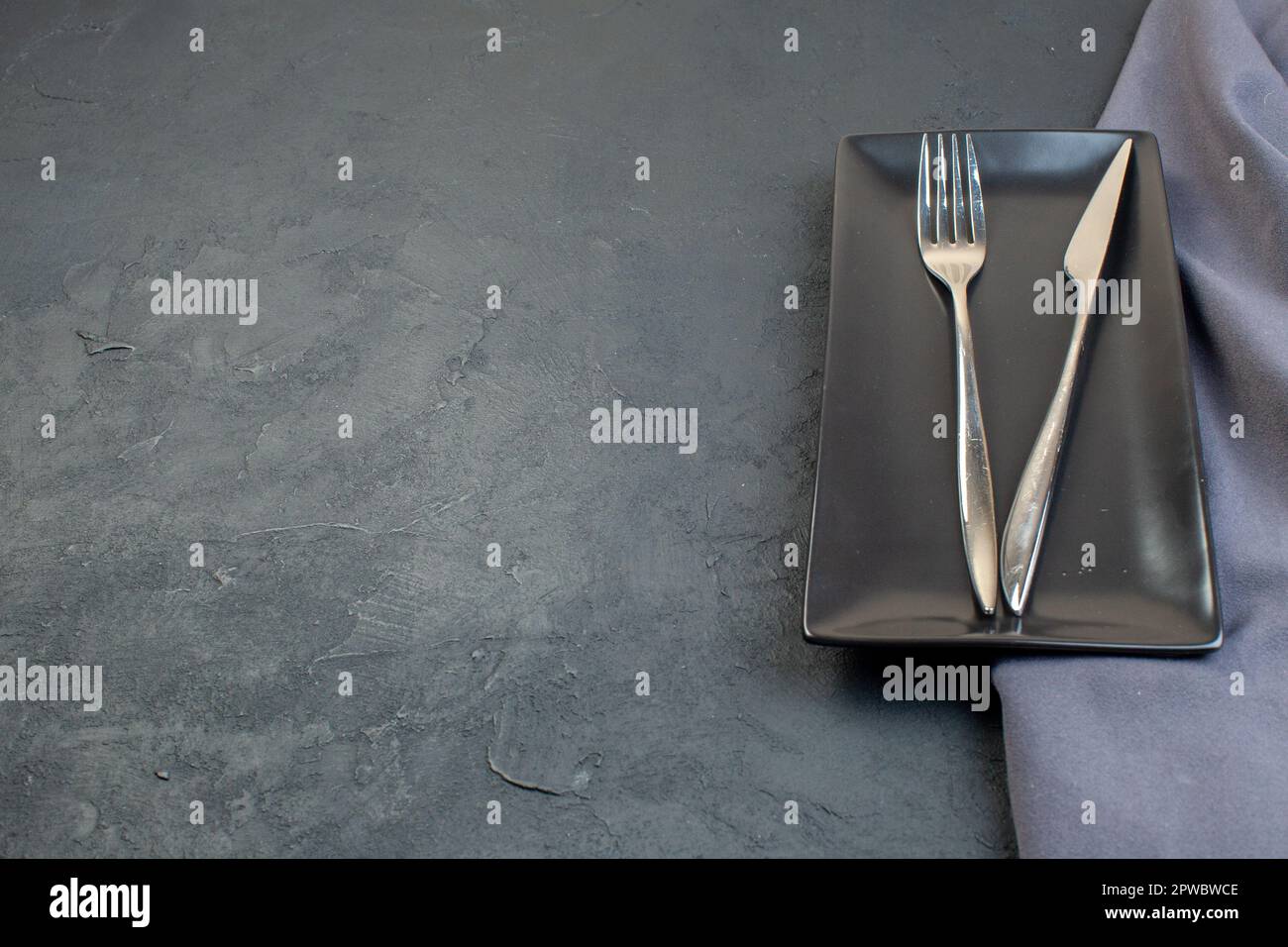 front view long black plate with fork and knife inside on dark ...