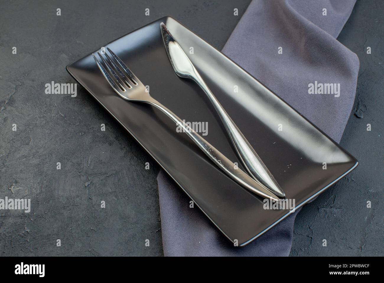front view long black plate with fork and knife inside on dark ...