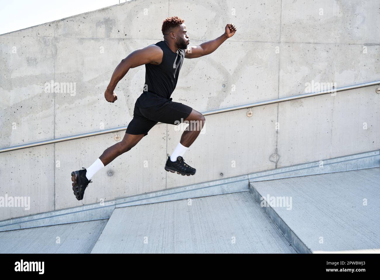 Confident strong fit sporty young black man running along urban wall ...
