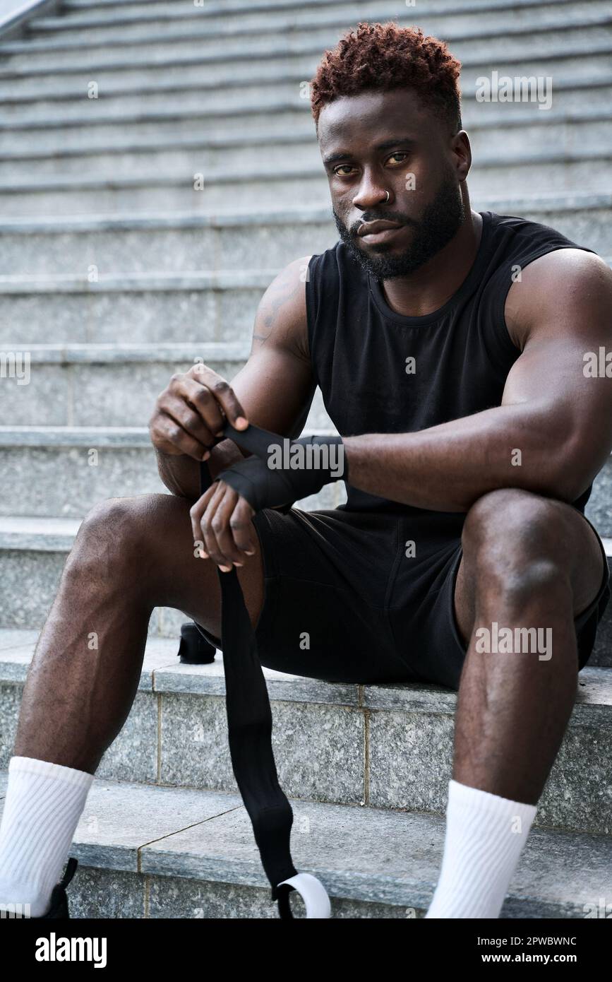 Sporty young black man sitting at urban stairs wrapping hands with ...