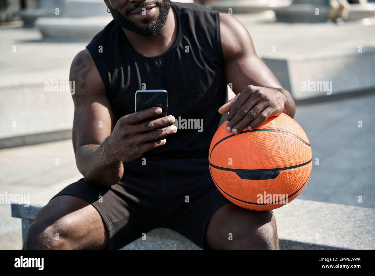 Fit sporty young black man holding basketball ball using phone outdoors ...