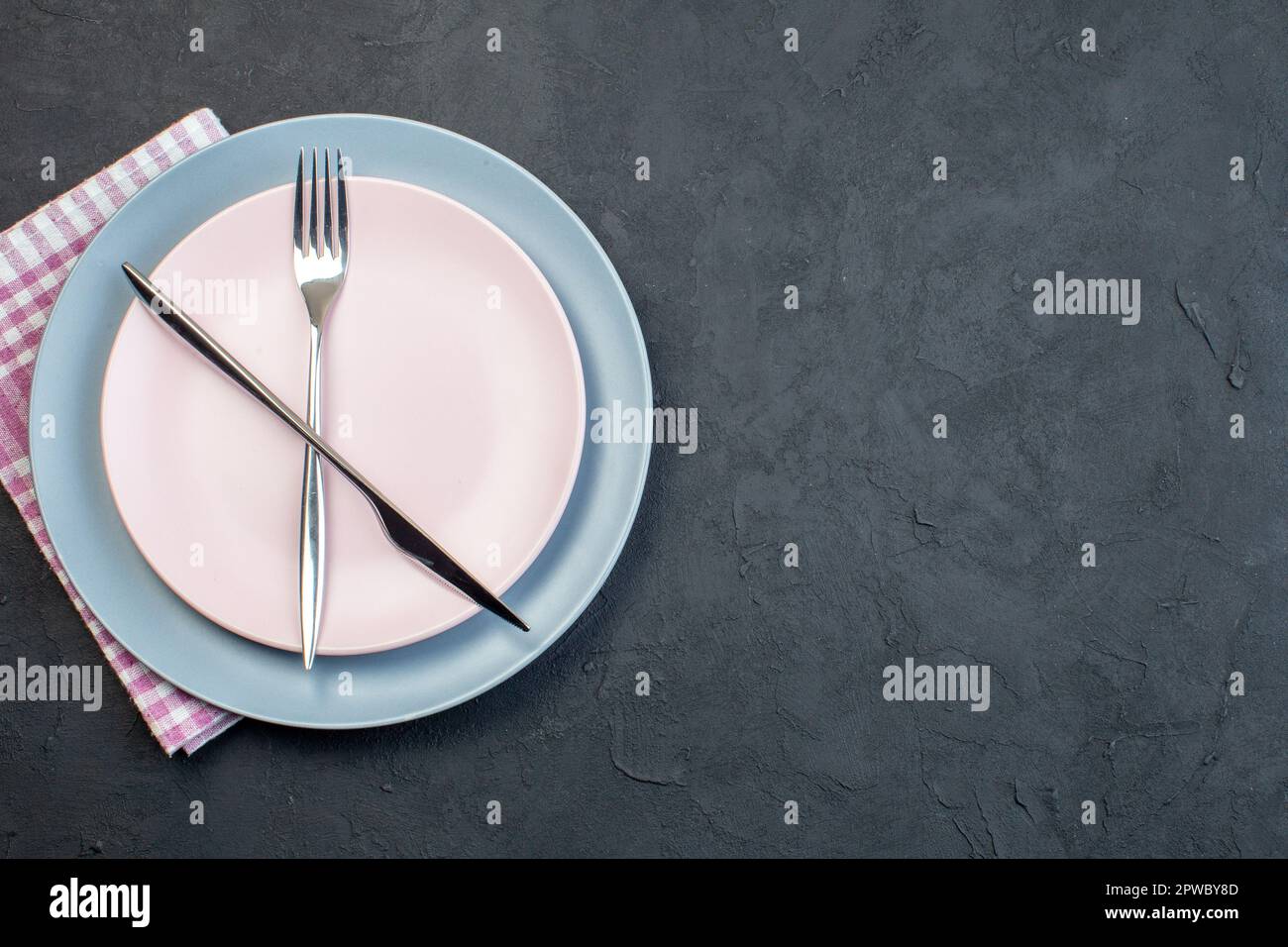 top view elegant pink plate with blue plate knife and fork on dark ...