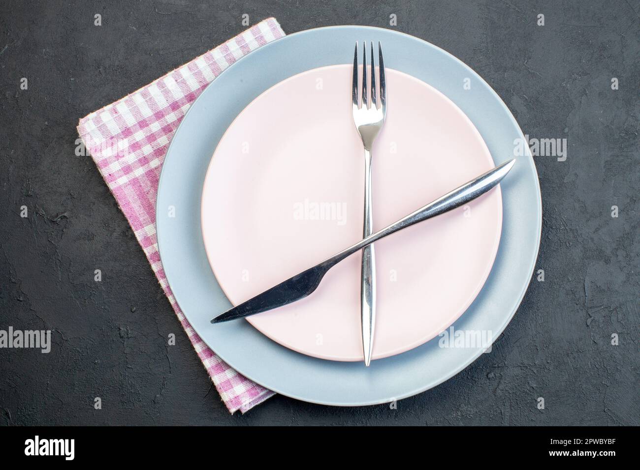 top view elegant pink plate with blue plate knife and fork on dark ...