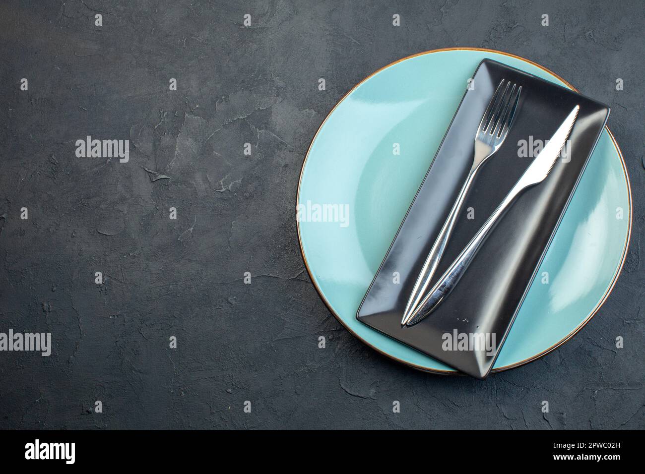 top view long black plate with blue plate fork and knife on dark ...