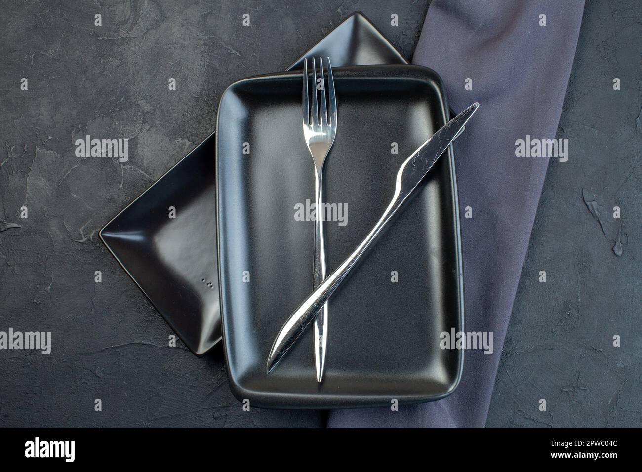 top view long black plate with fork and knife inside on dark background ...