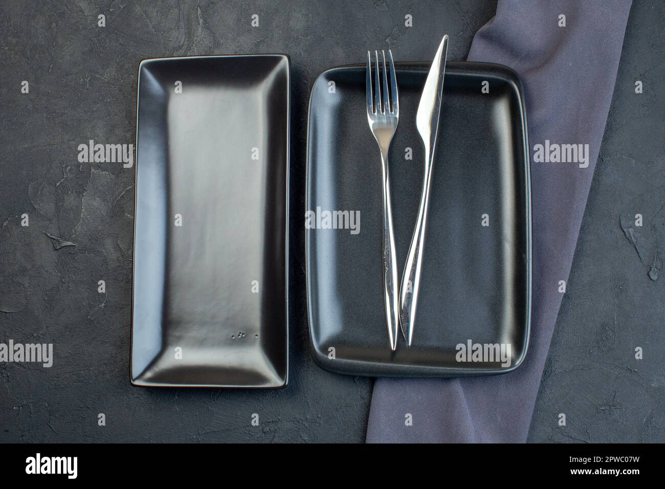 top view long black plate with fork and knife inside on dark background ...