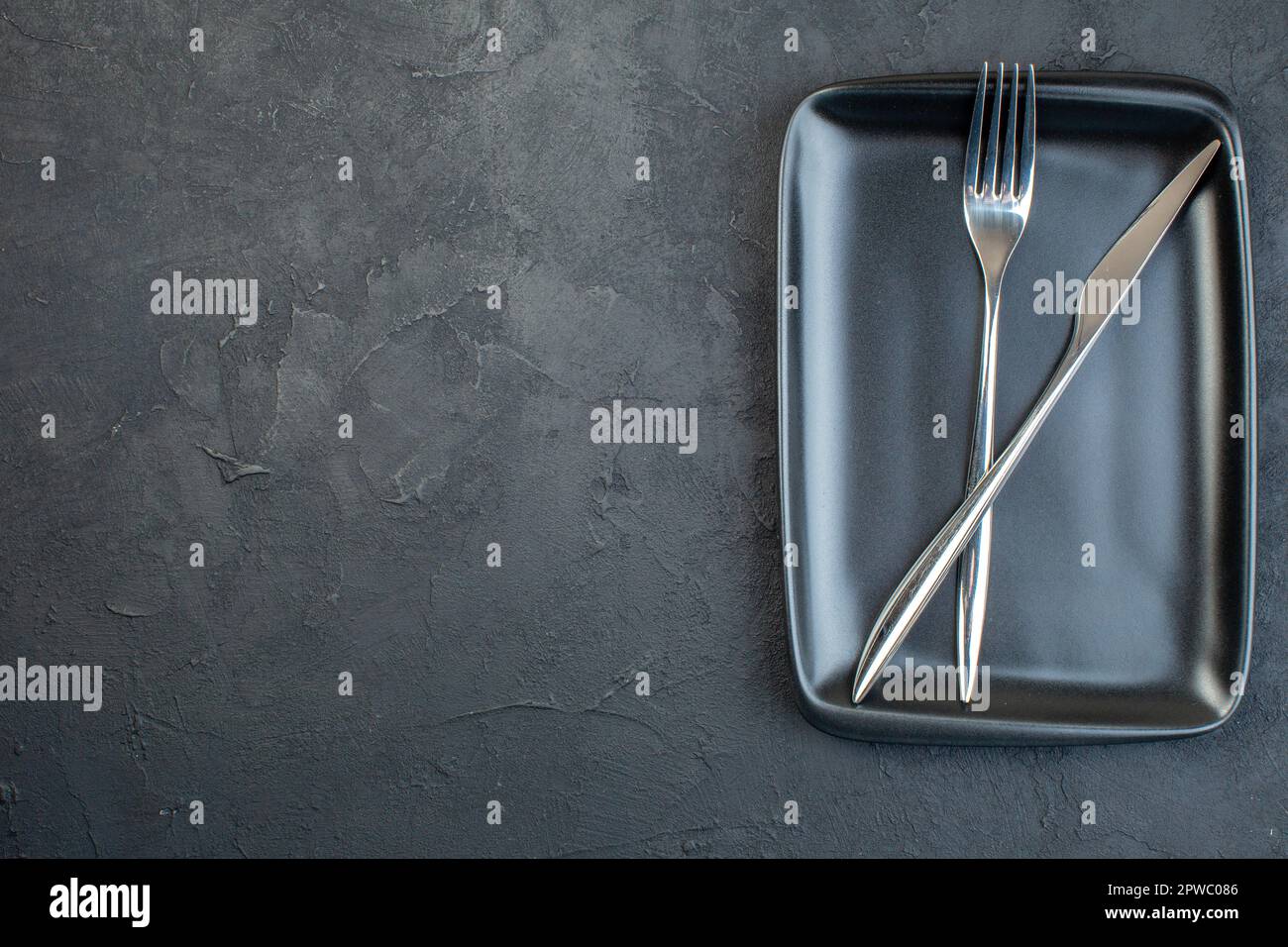 top view long black plate with fork and knife inside on dark background ...