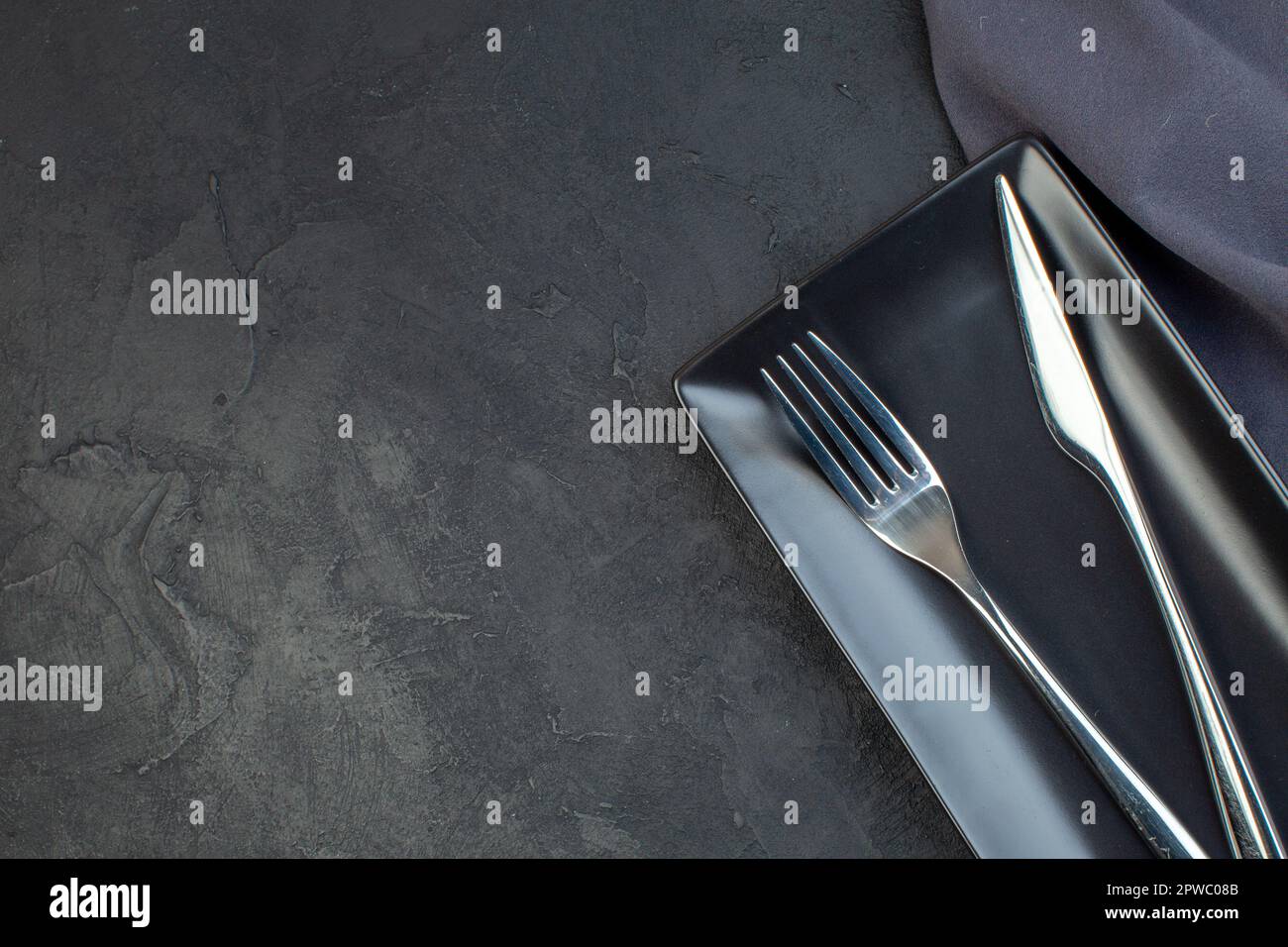 top view long black plate with fork and knife inside on dark background ...