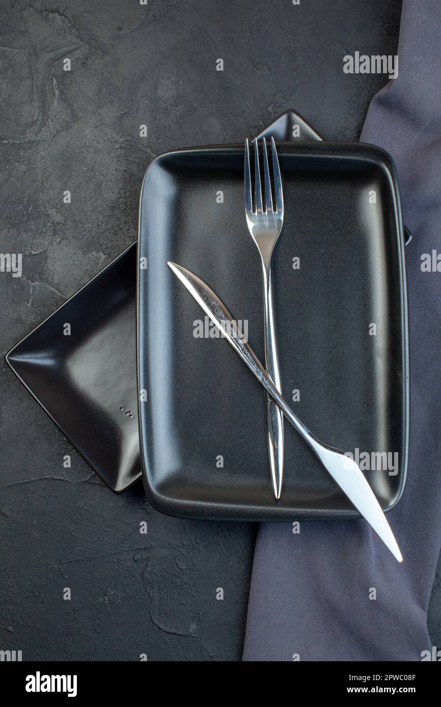top view long black plate with fork and knife inside on dark background ...