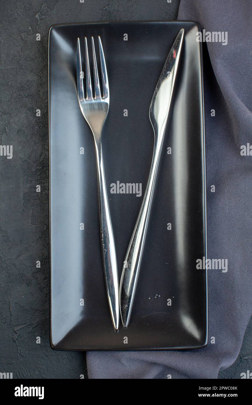 top view long black plate with fork and knife inside on dark background ...