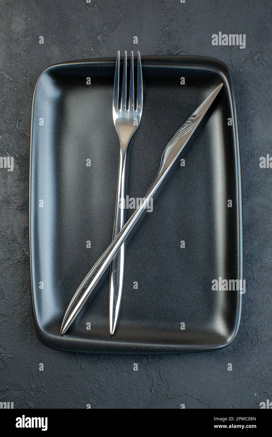 top view long black plate with fork and knife inside on dark background ...