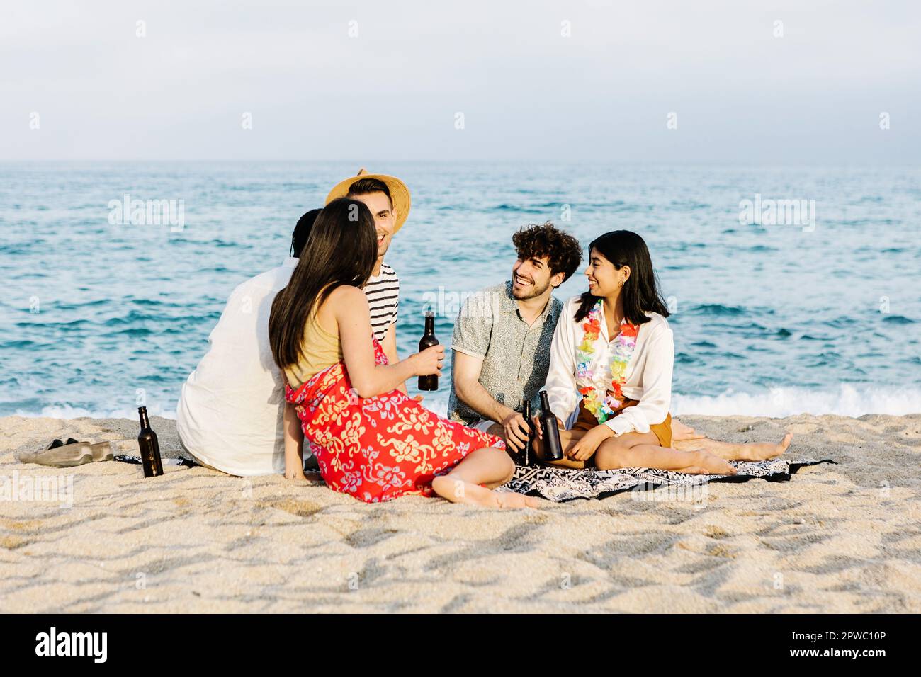 Happy young friends social gathering sitting on the beach in summer ...