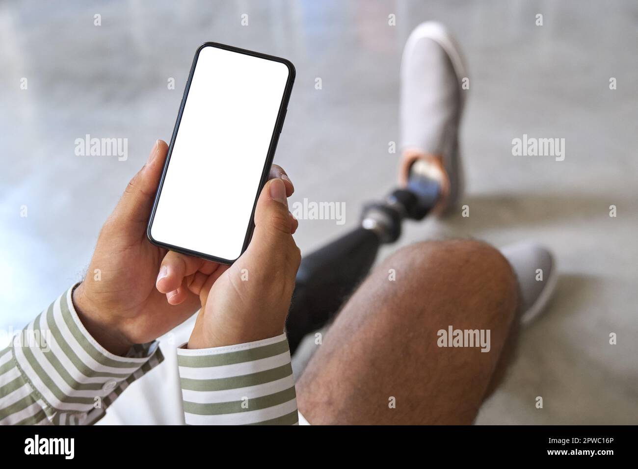 Amputee man with leg prosthesis sitting on sofa at home using phone ...
