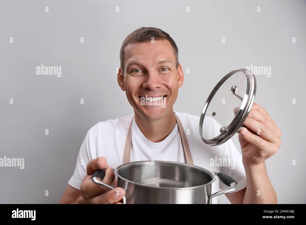 Happy man with cooking pot on light grey background Stock Photo - Alamy