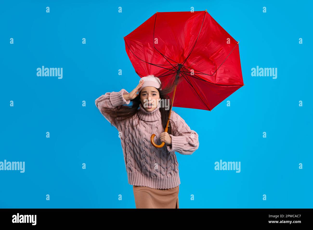 Emotional woman with umbrella caught in gust of wind on light blue ...