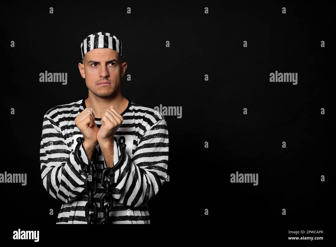 Prisoner in striped uniform with chained hands on black background ...