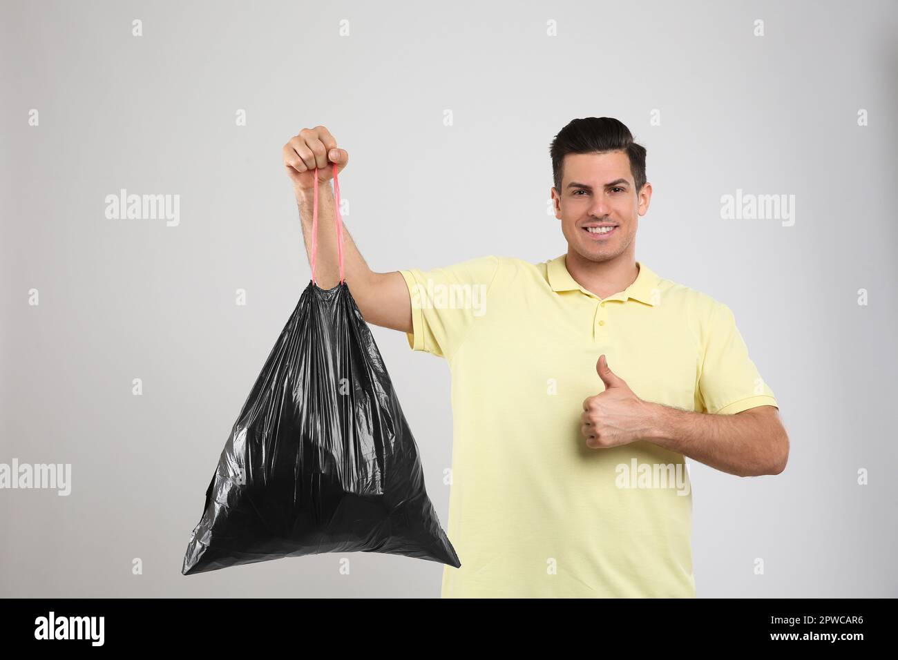 Man holding full garbage bag on light background Stock Photo - Alamy