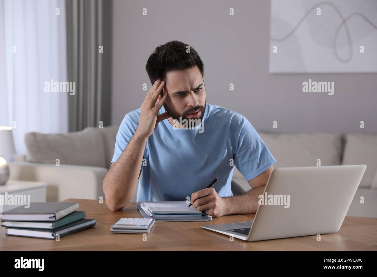 Confused young man watching webinar at table in room Stock Photo - Alamy