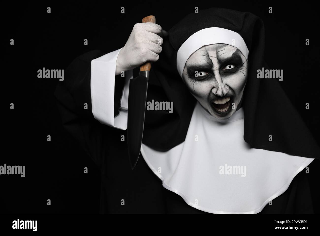 Scary devilish nun with knife on black background. Halloween party look ...