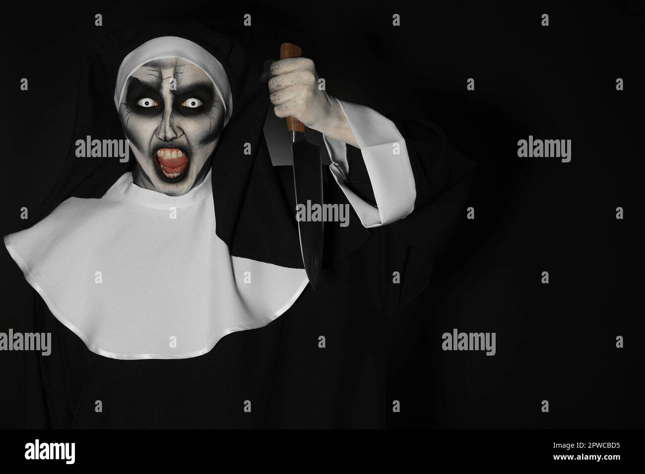 Scary devilish nun with knife on black background, space for text ...