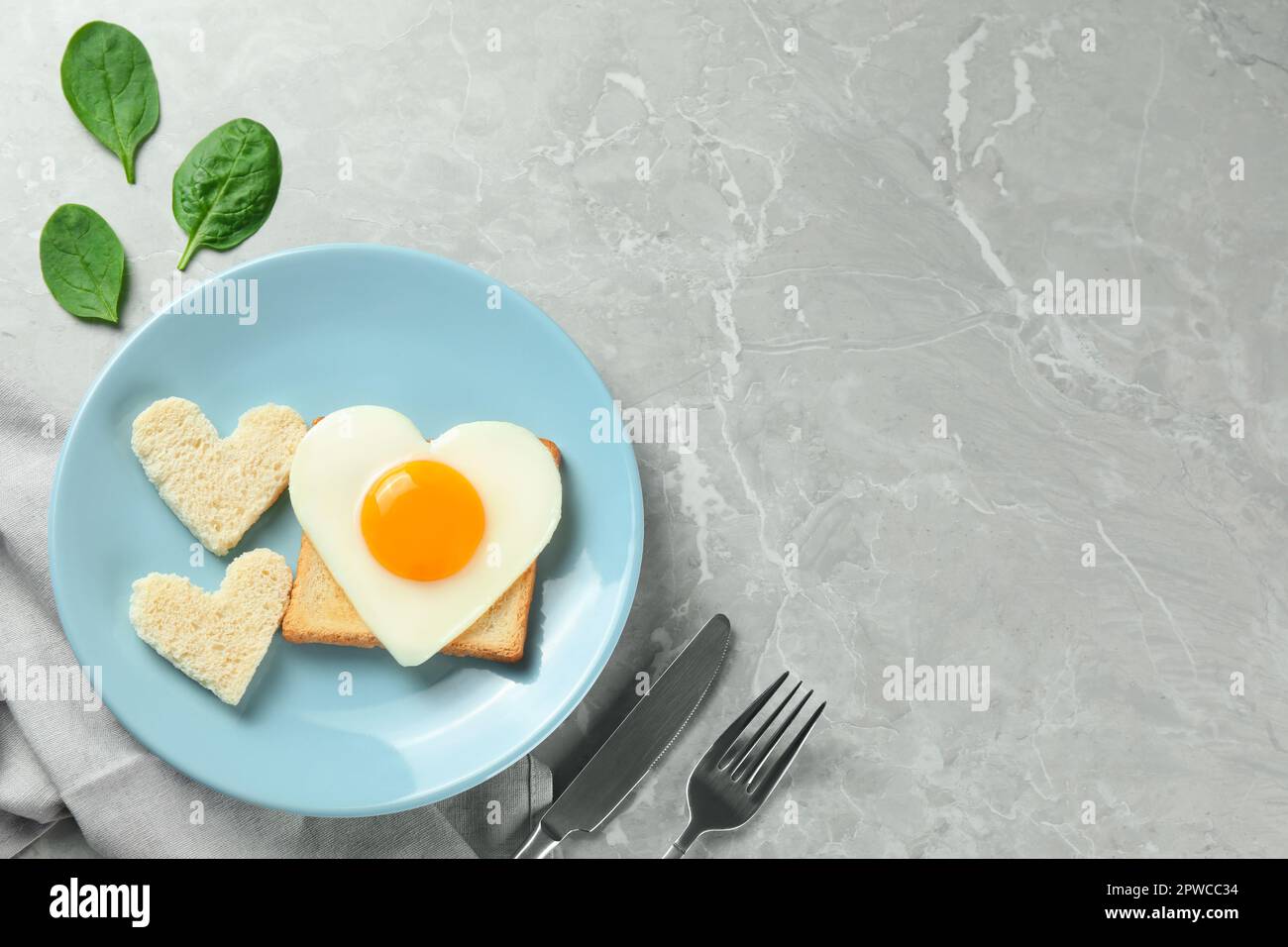 Romantic breakfast with heart shaped fried egg on served grey marble table, flat lay. Space for ...
