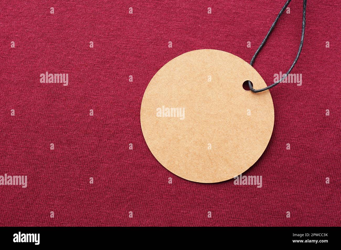 Circle shaped tag with space for text on dark red fabric, top view ...