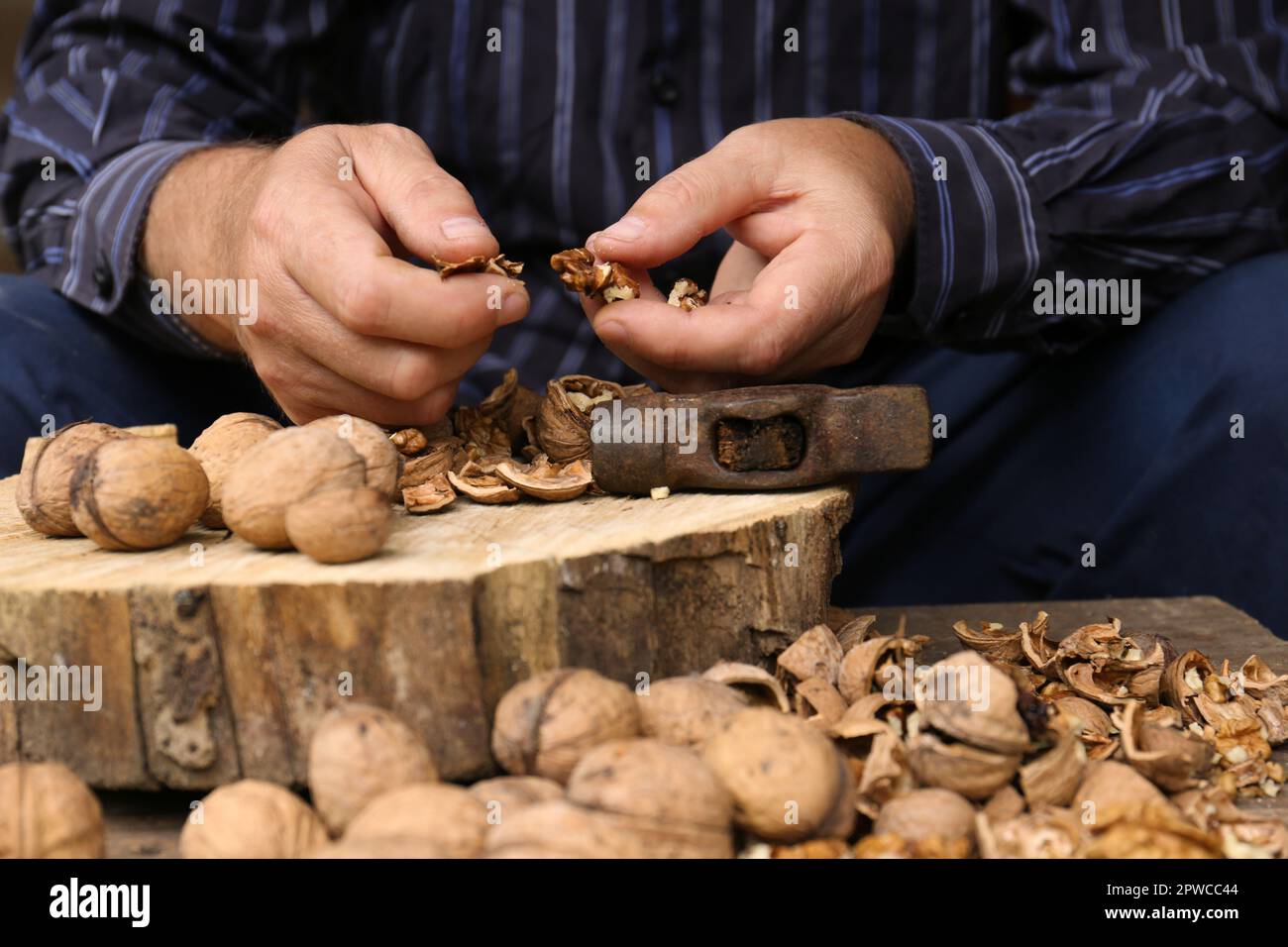 Man cracking walnuts with hammer at wooden table, closeup Stock Photo ...