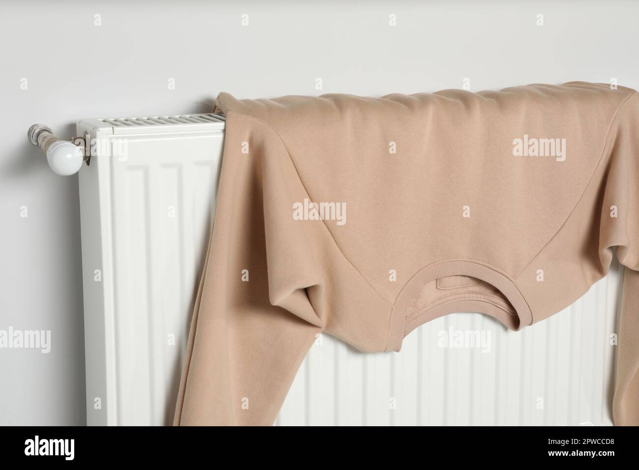 Clean beige sweatshirt on heating radiator near white wall Stock Photo ...