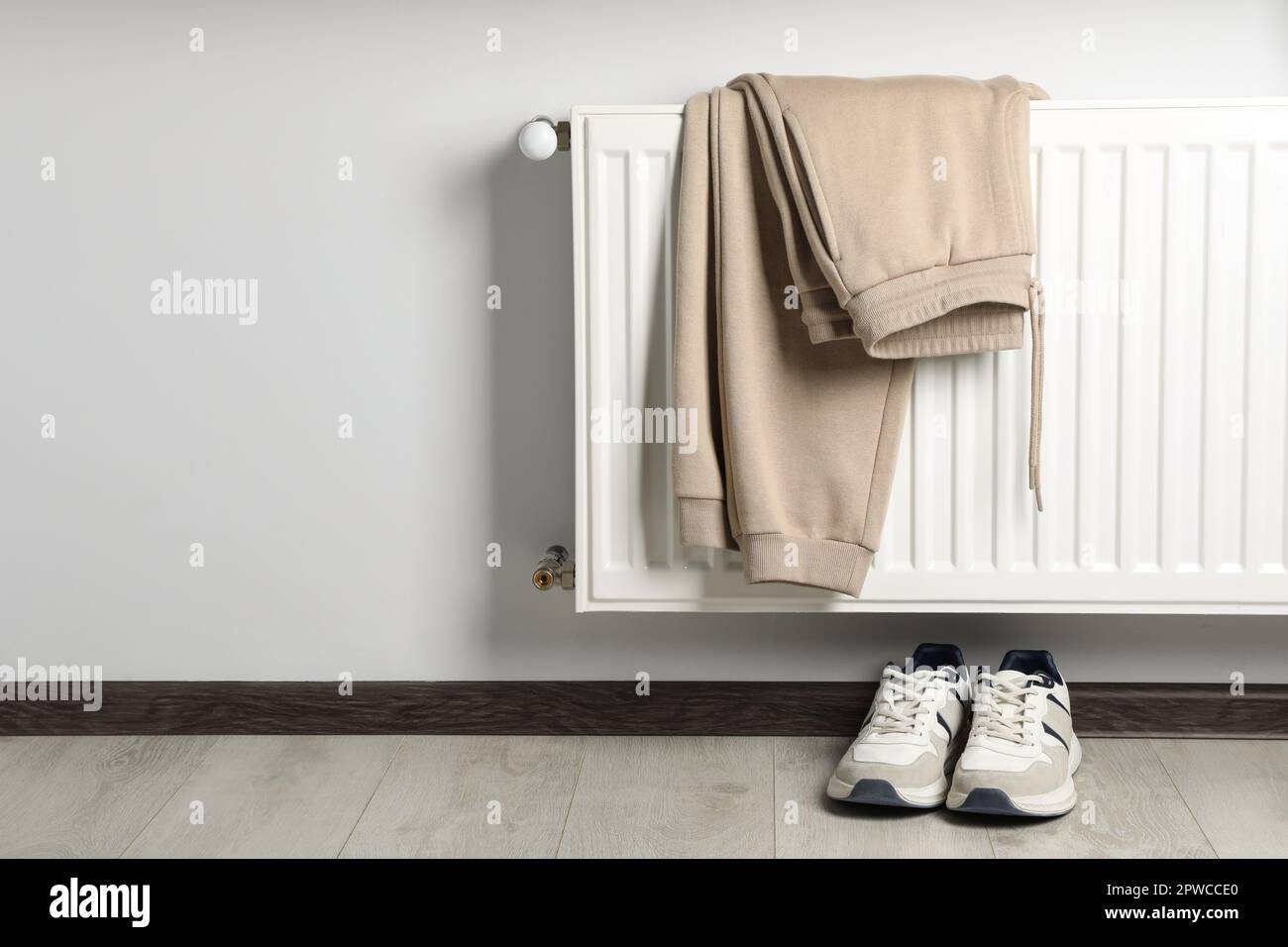 Heating radiator with beige pants and sneakers indoors. Space for text ...